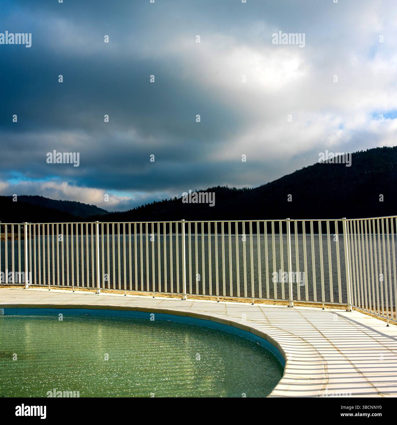 A serene lake reflects the overcast sky, with gentle ripples on the ...