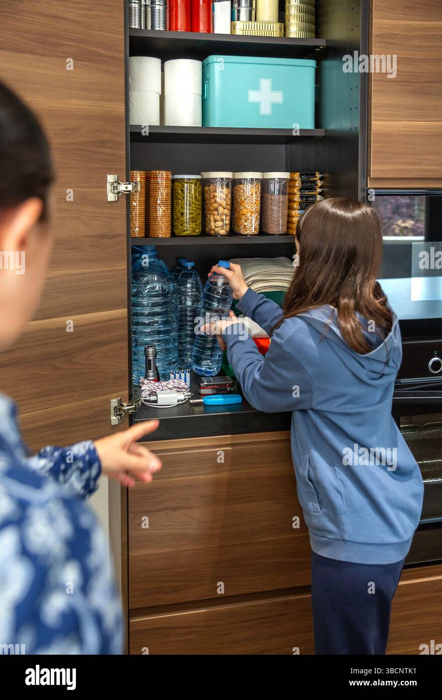 Mother and daughter storing water bottles and food in pantry for ...