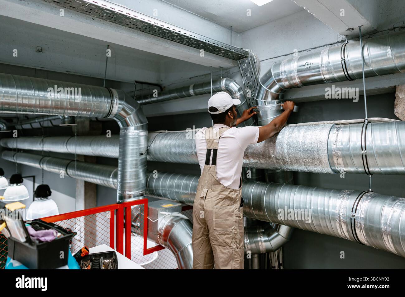 Worker installing ventilation ductwork in industrial setting during ...