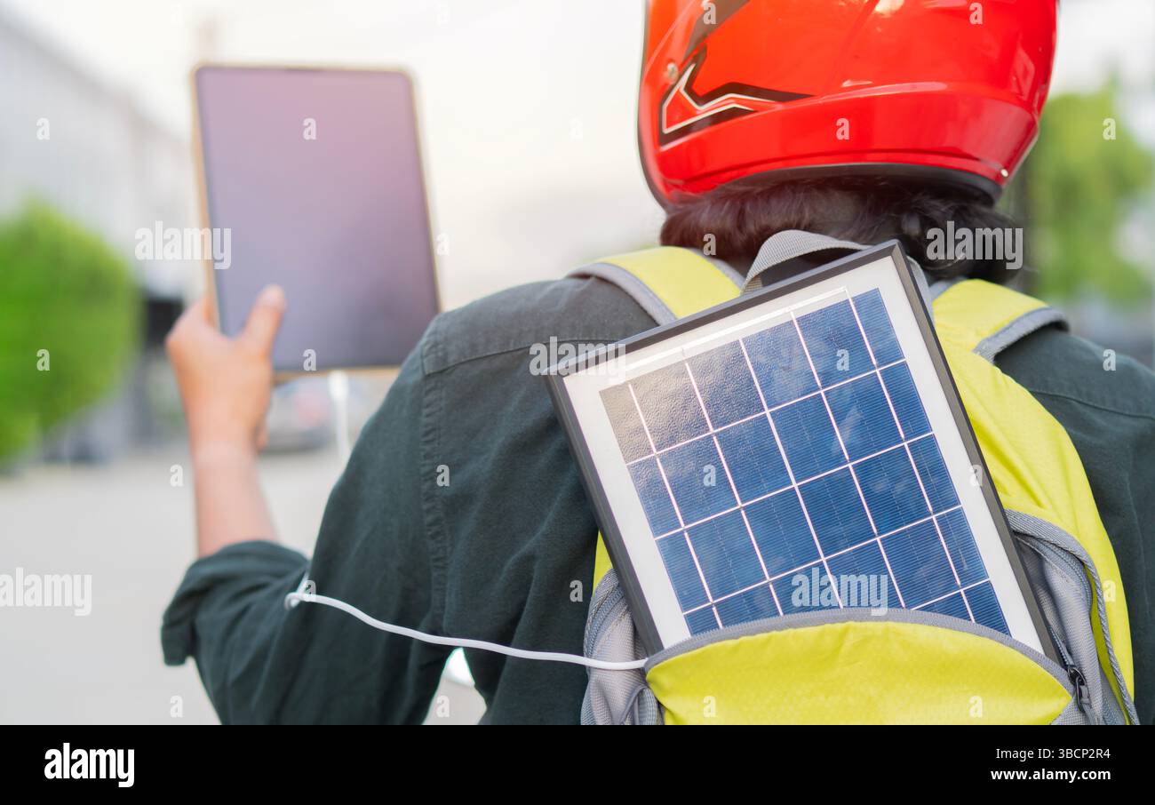 Back view of man with portable solar panel in backpack and tablet while ...