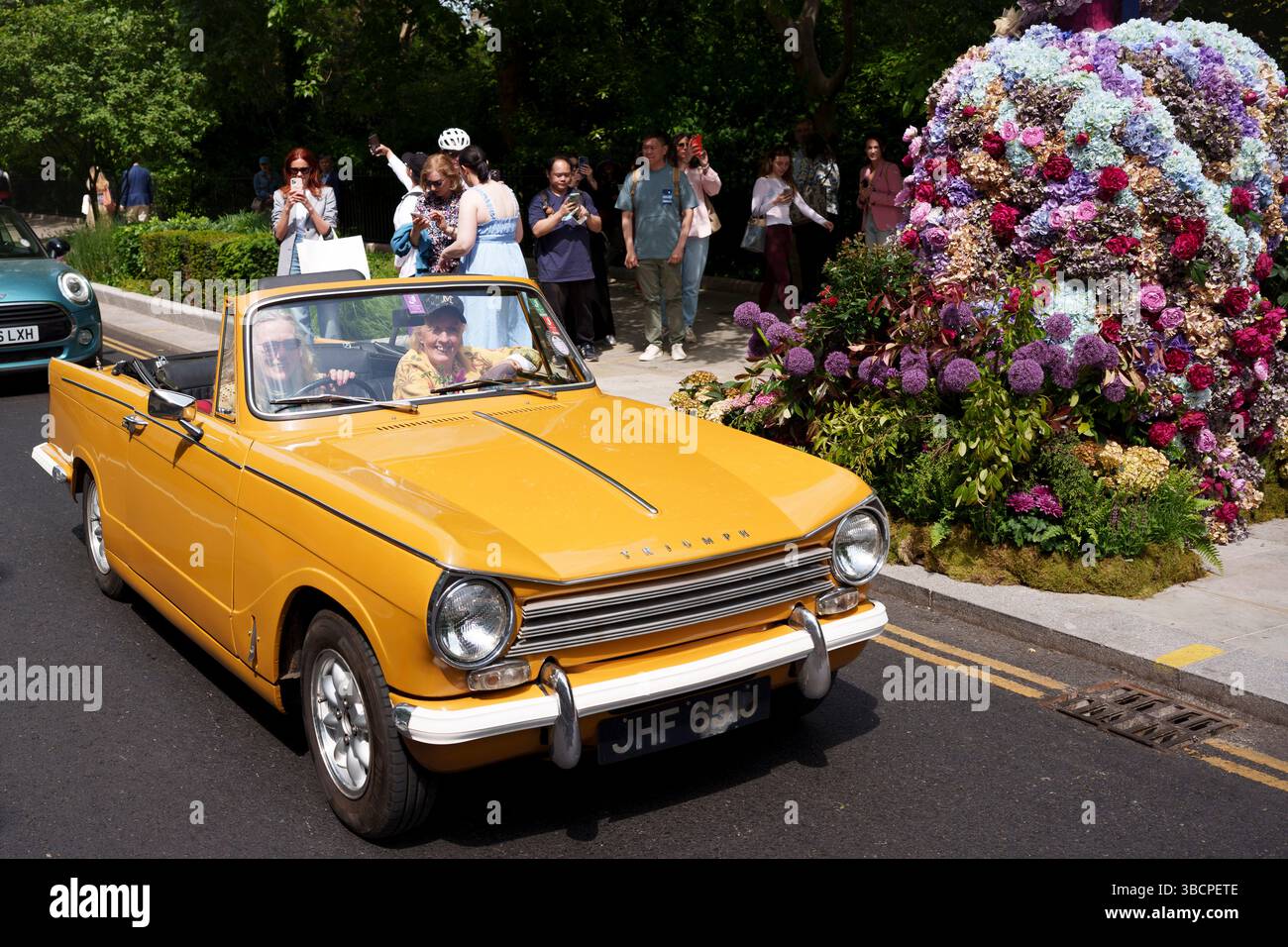 A vintage Triumph Herald car is driven past a festival theme of flowers ...