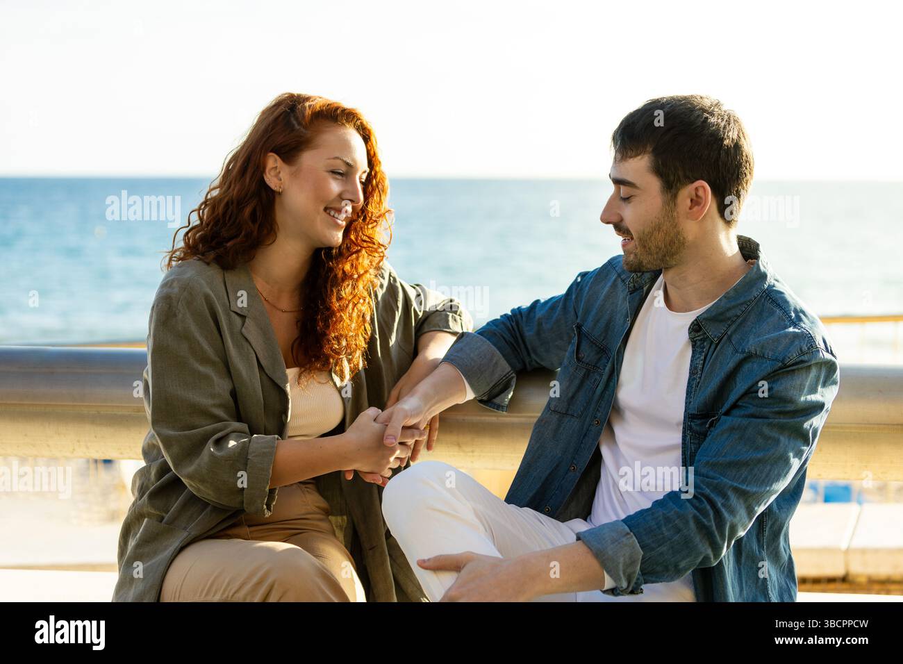 Man and woman sitting close together near the sea, holding hands and ...