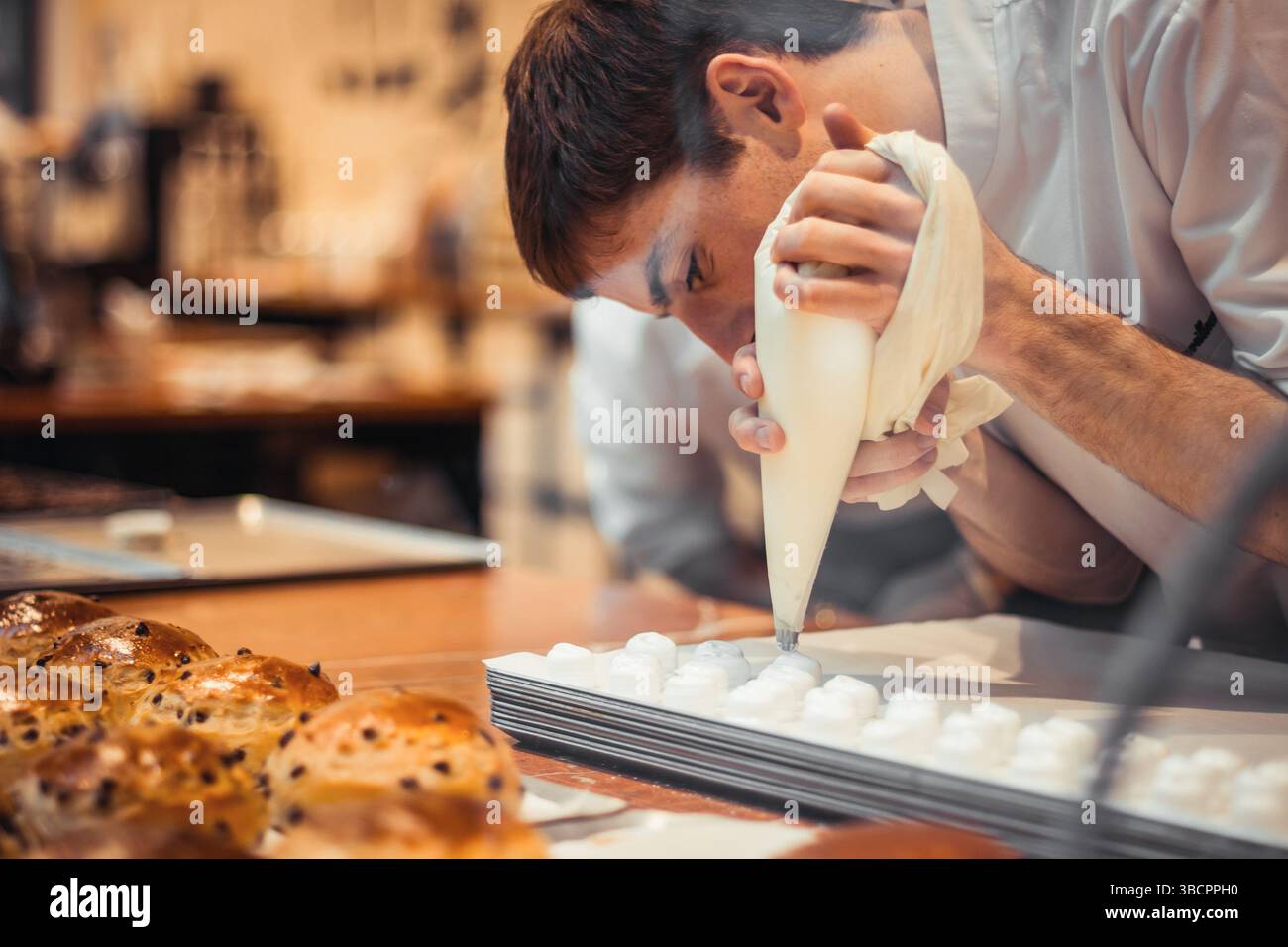 Man in white chef's blouse piping meringue dessert using conic pastry ...