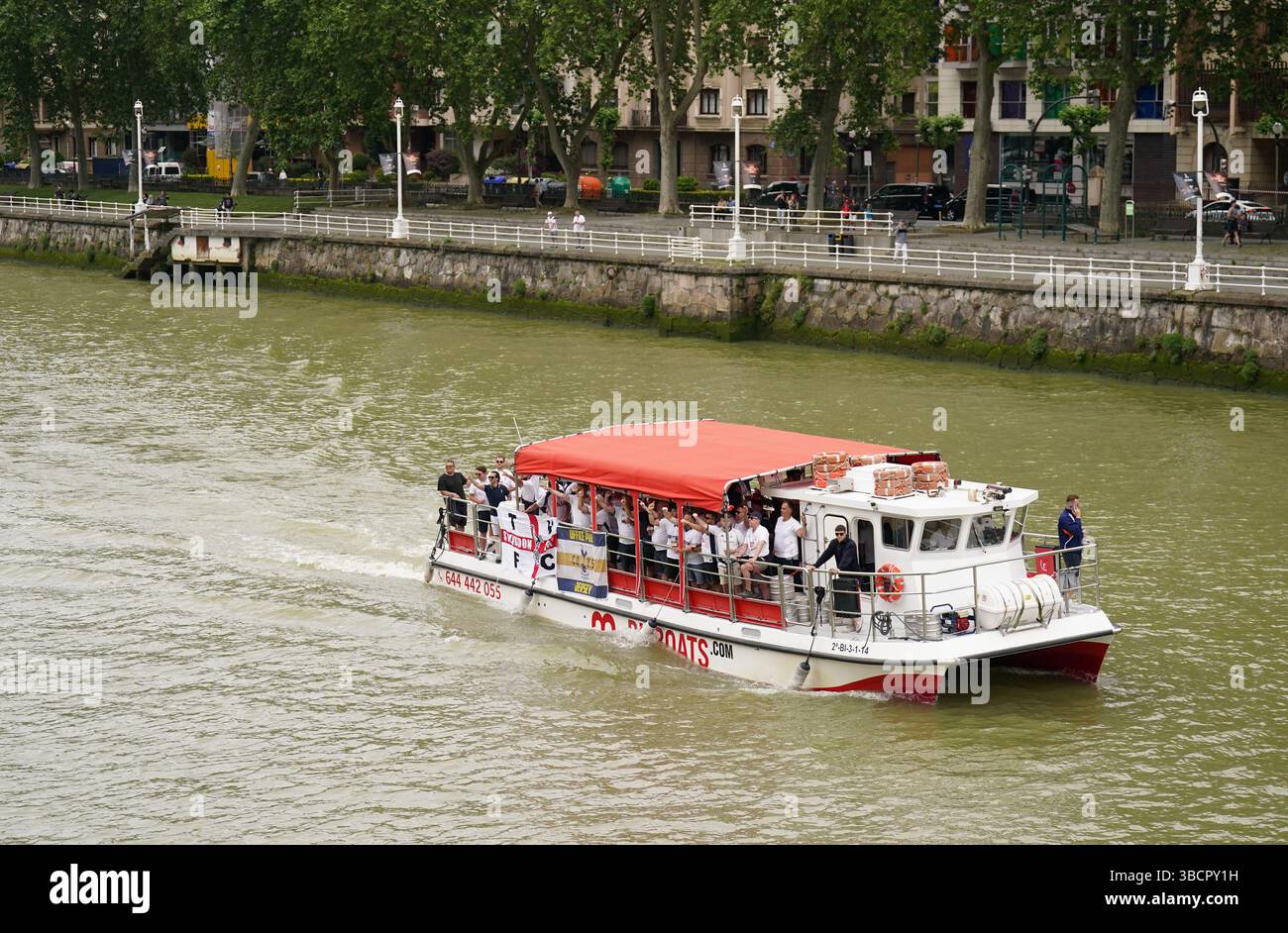 A boat full of Tottenham Hotspur fans heads down the Nervion River in ...