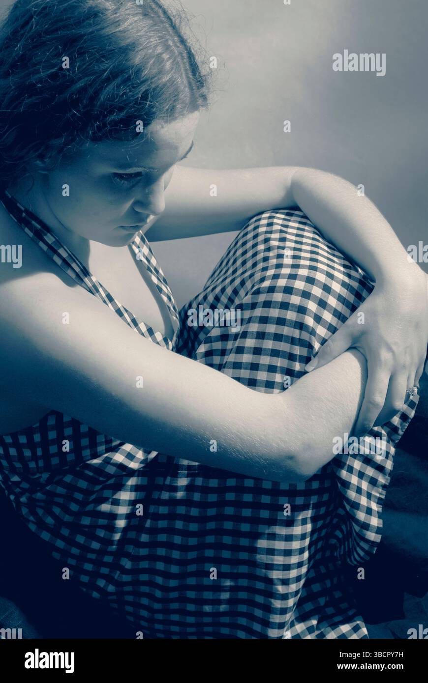 Depressed young woman looking down with arms wrapped around knees. USA ...