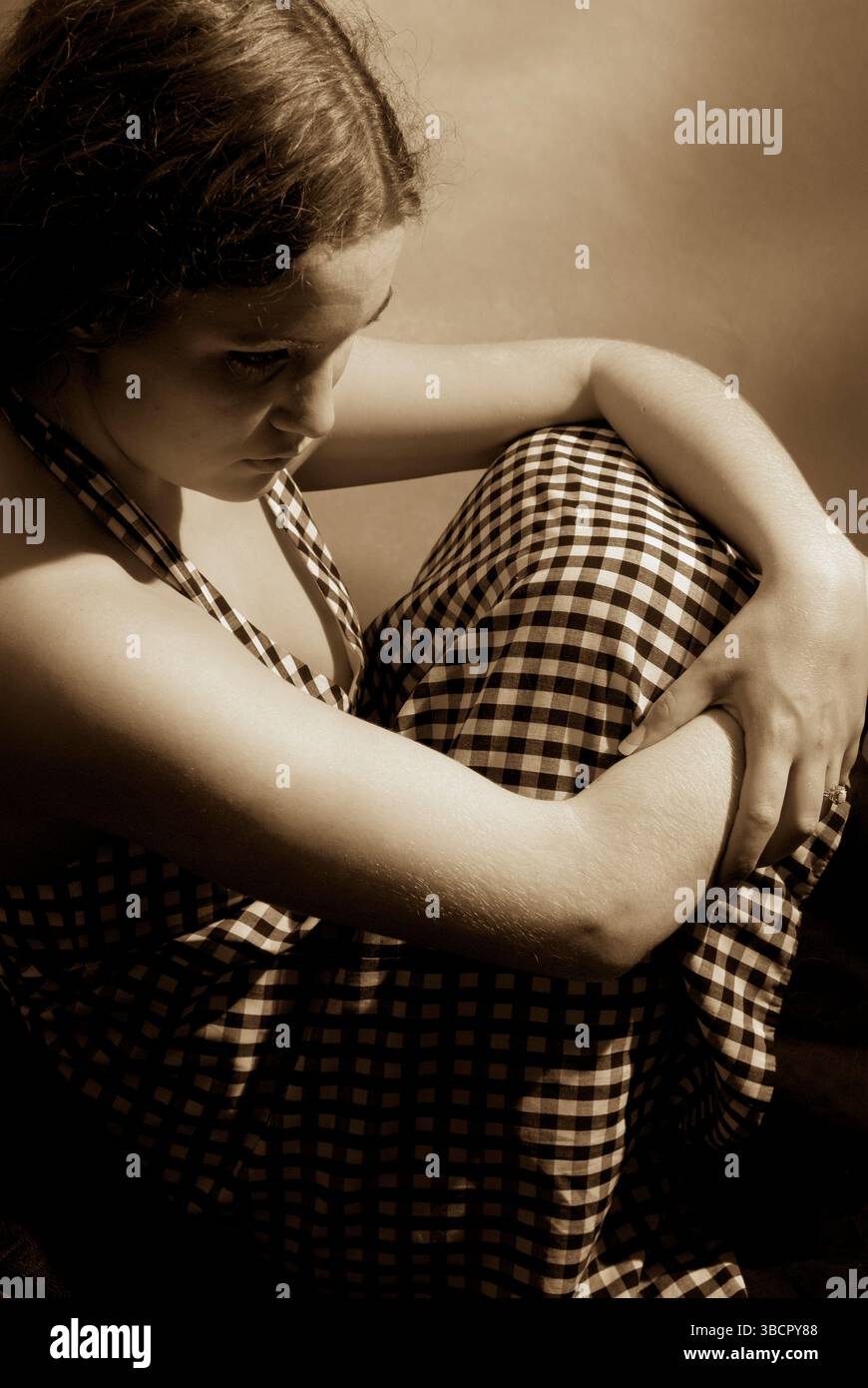 Depressed young woman sitting with arms wrapped around her knees ...