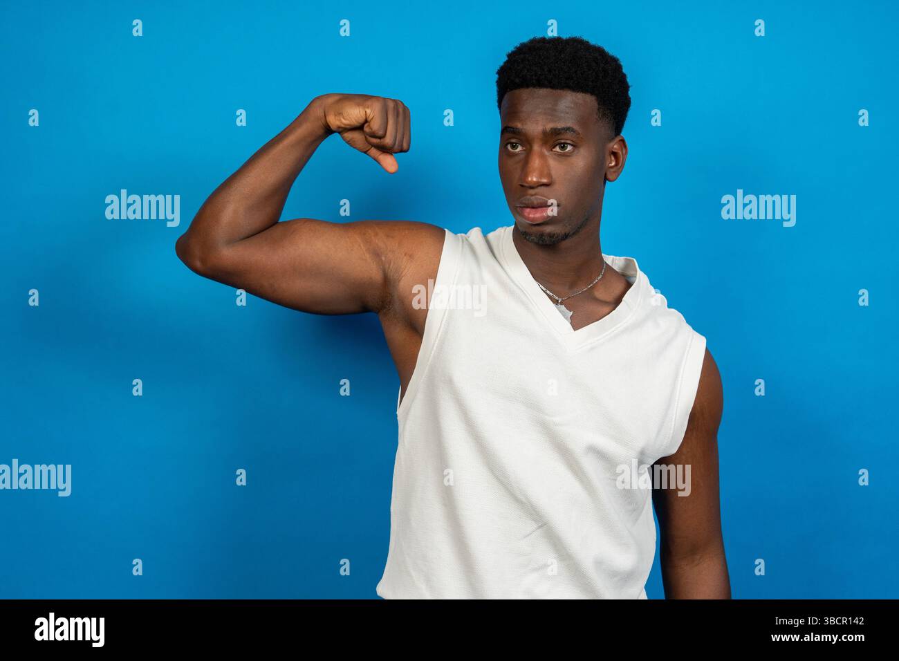 Strong sportsman flexing biceps while wearing white shirt on blue ...