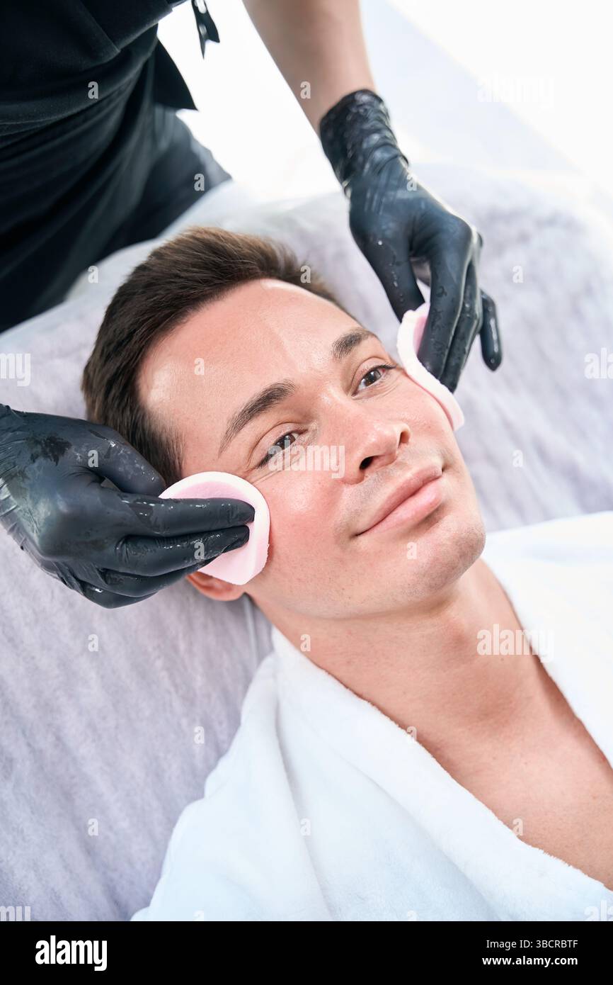 Female therapist and male patient having facial treatment cleaning face ...