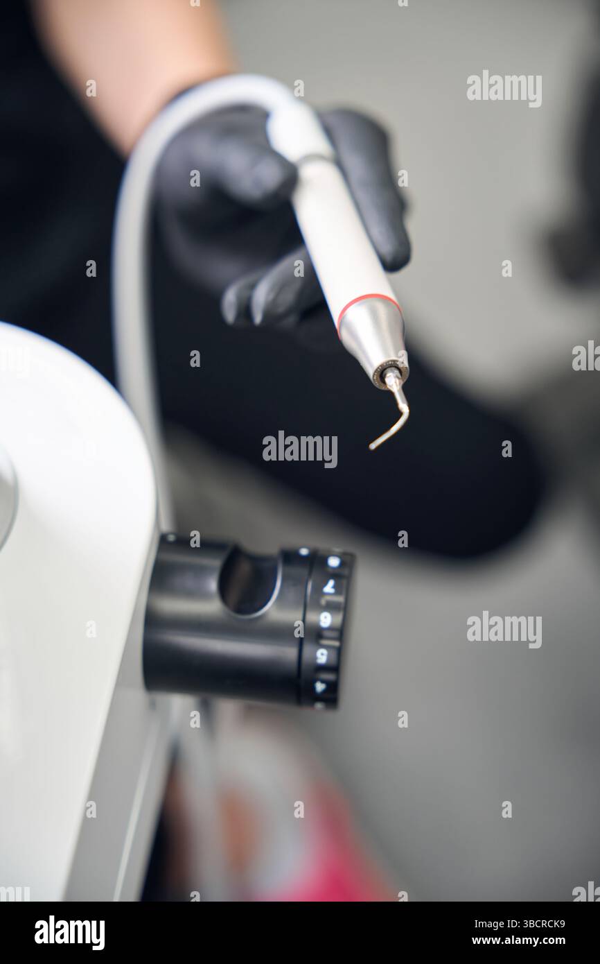 Female dentist adjusting speed of scaler before starting patient teeth ...