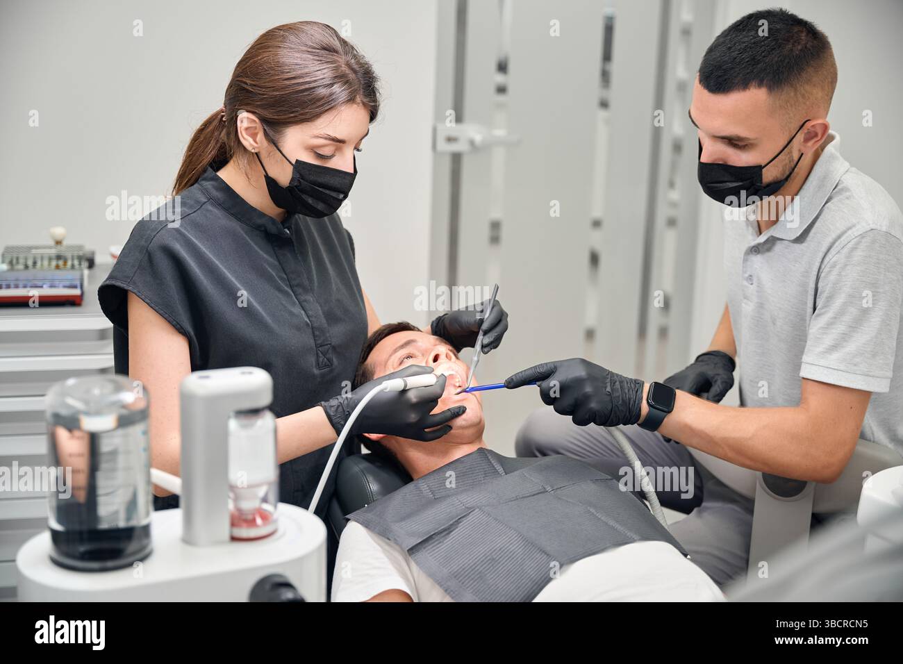 Dentist assistant holding saliva ejector while doctor treating client's ...