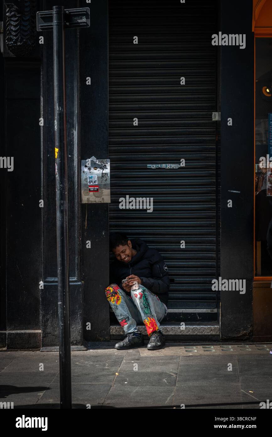 a man sat on a door step near Chinatown London reading his messages ...
