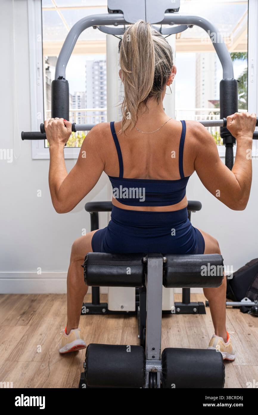 46 year old Brazilian woman doing a lat pulldown on the pulley machine ...