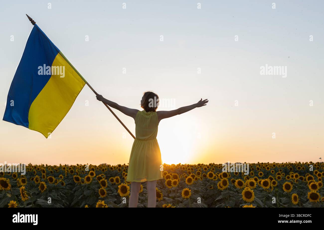 Ukrainian flag in hand of woman, standing with back against backdrop of ...