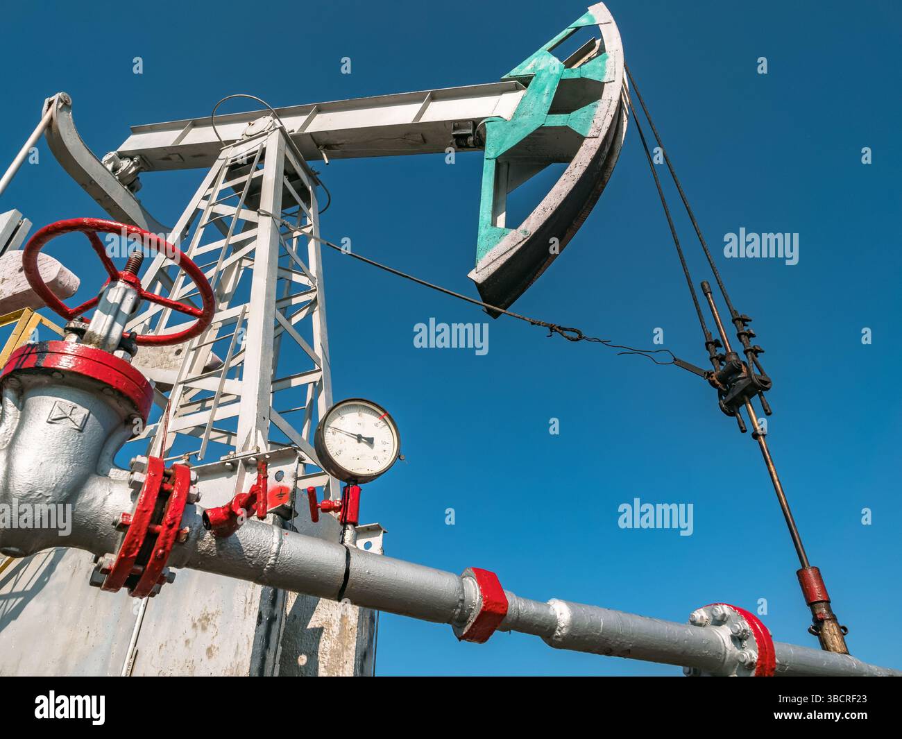 Oil pump jack operating under clear blue sky at oil field during ...