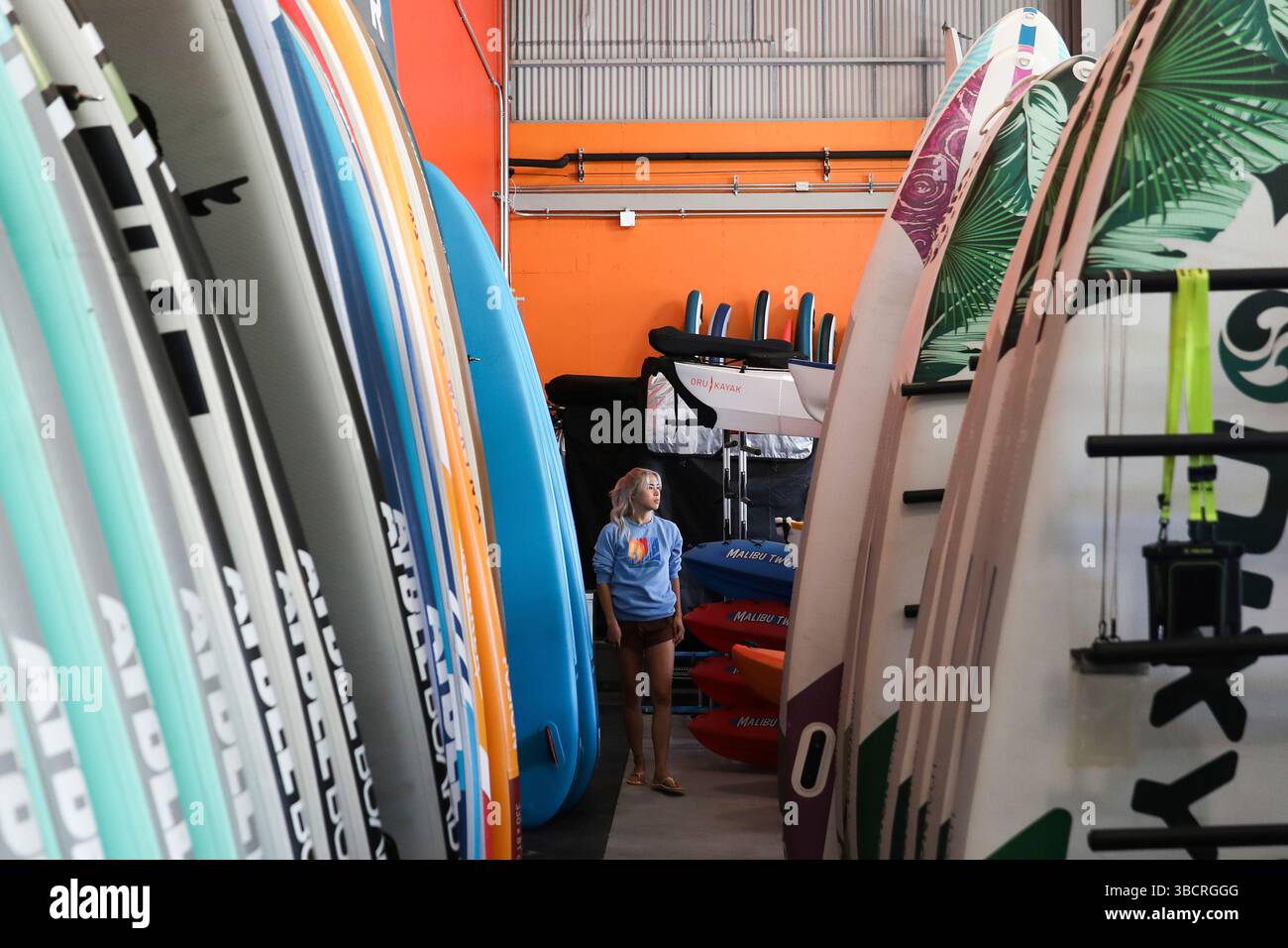 Dogpatch Paddle employee Sarah Chin walks past a row of paddle boards ...