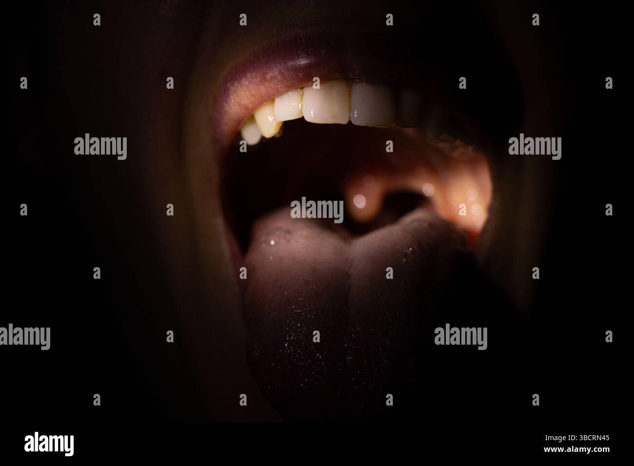 Open mouth of a girl in the dark with a beam of light in the mouth with ...