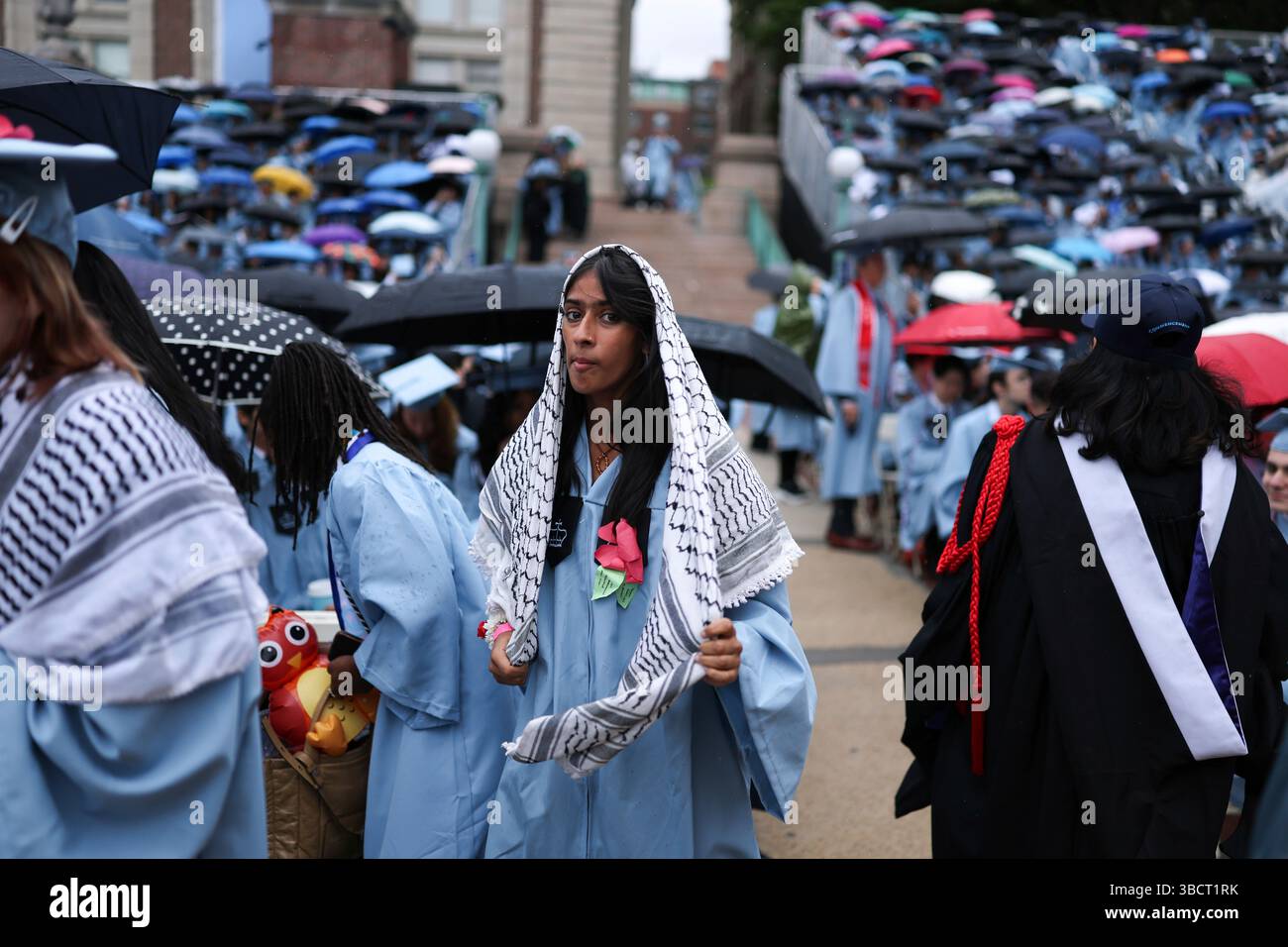 A student wears a keffiyeh scarf as she walks past other graduates ...