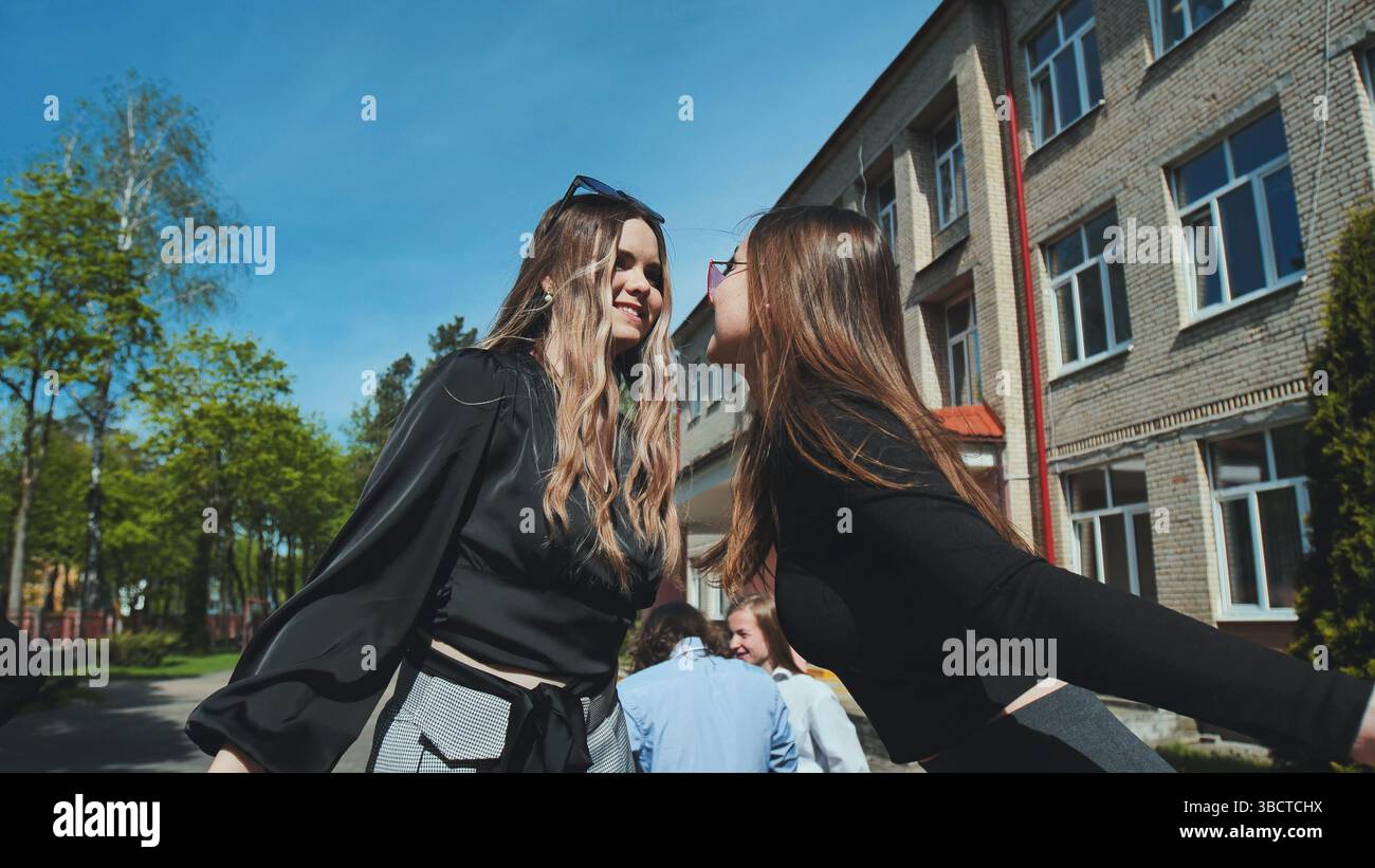 Two high school friends sharing a sweet kiss on the cheek to celebrate ...