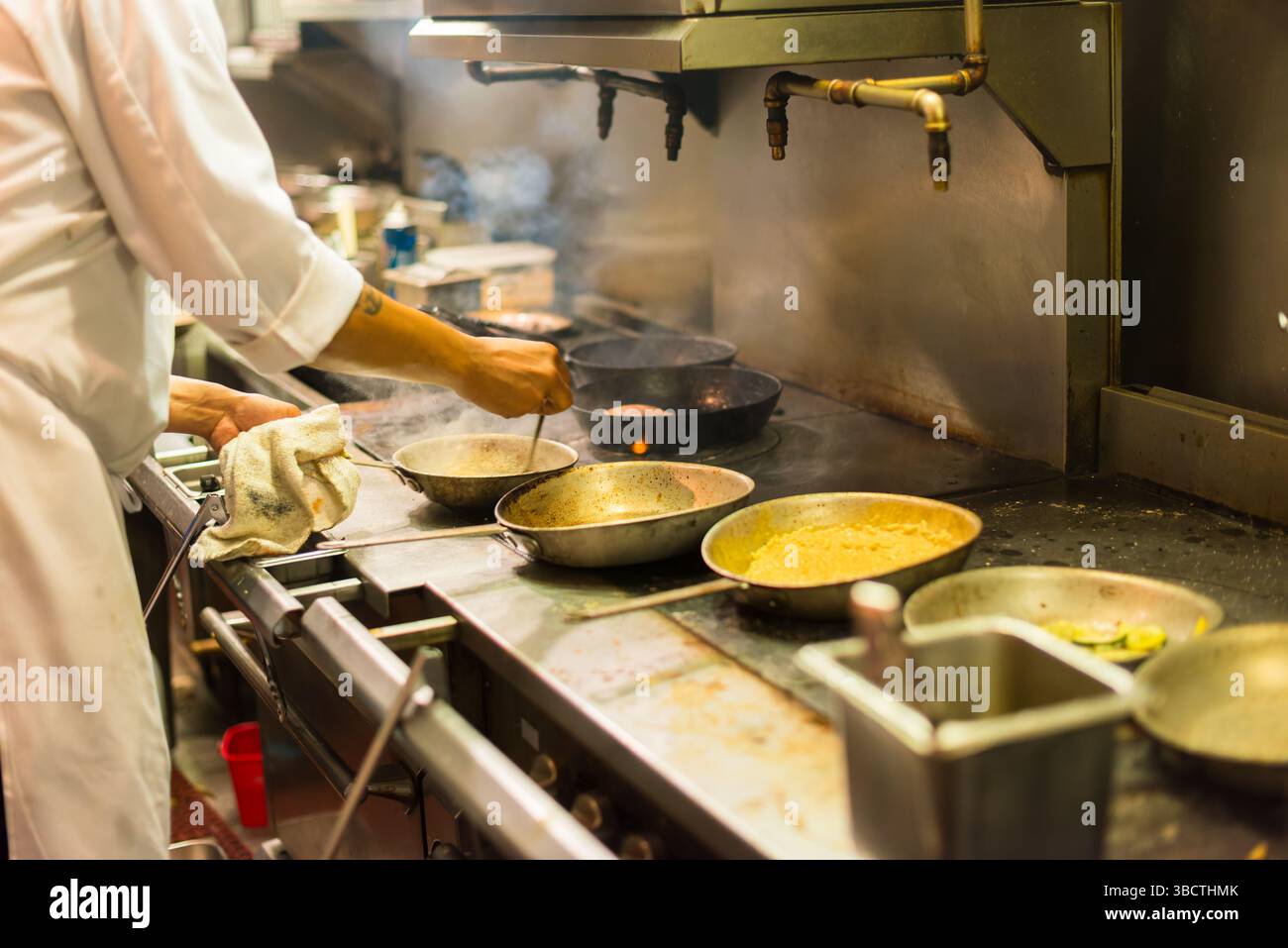 A professional chef manages multiple saucepans on a commercial range ...