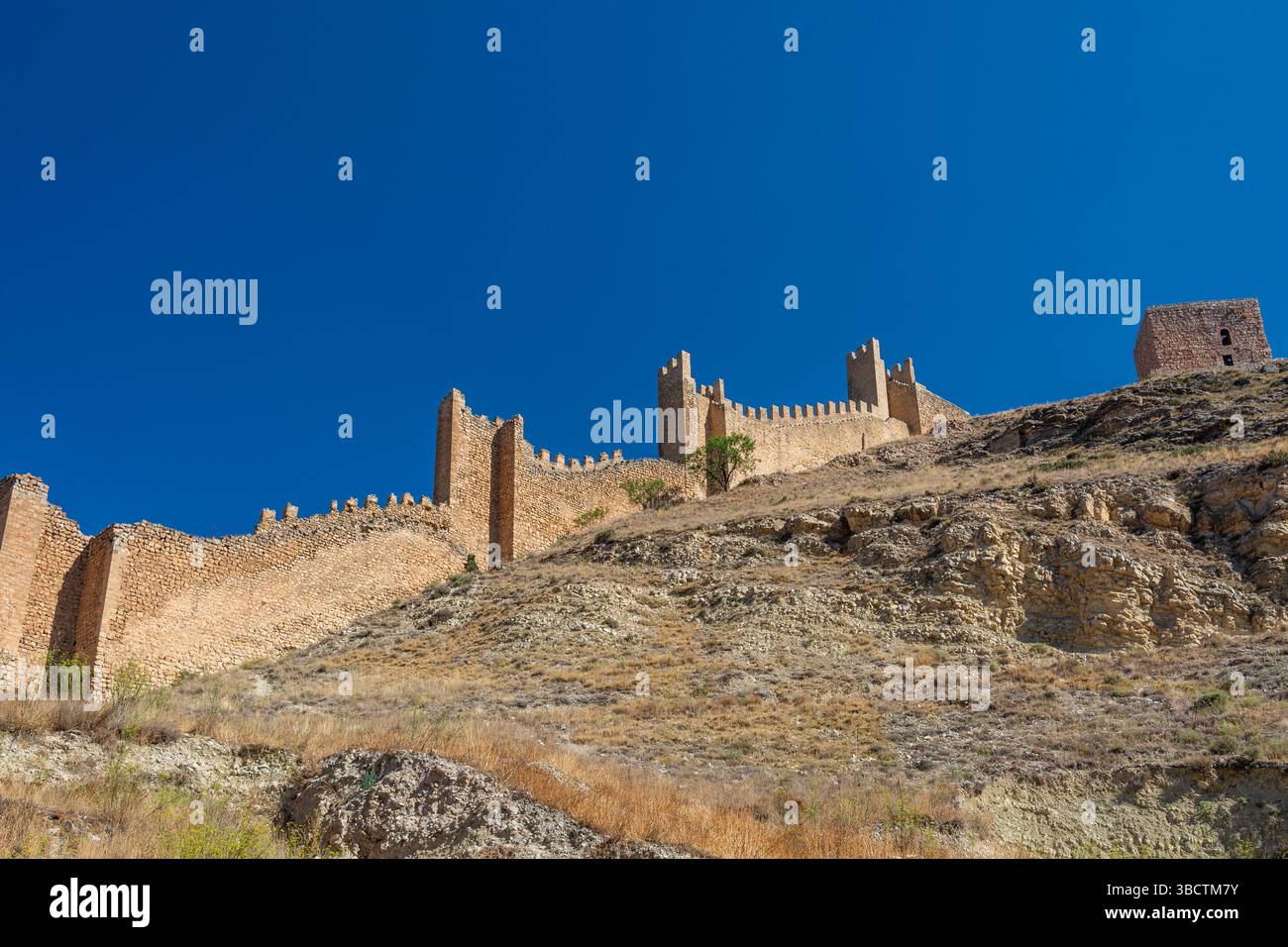 Historic medieval stone walls stretch across a rugged hillside beneath ...