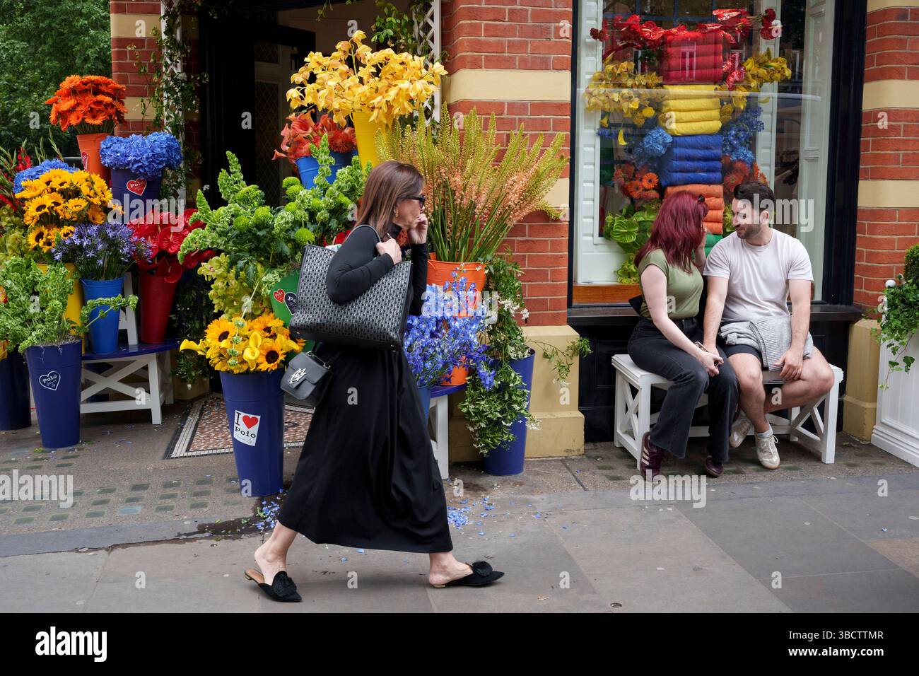 Shoppers sit outside a shop by the prime colours of flowers on display ...