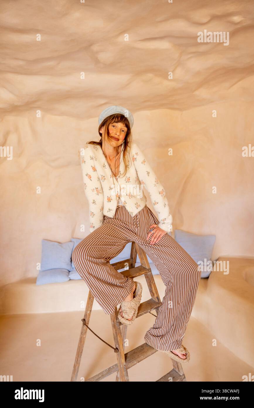 Woman sitting on a wooden ladder in a sculpted clay interior of a ...