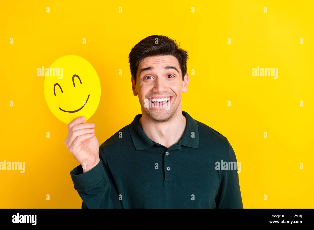 Young Man Smiling on Yellow Background Holding a Smiley Face Sign in a ...