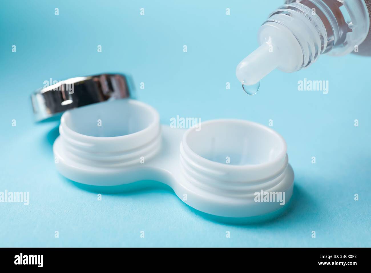 Dripping contact lens solution from bottle into case on light blue ...