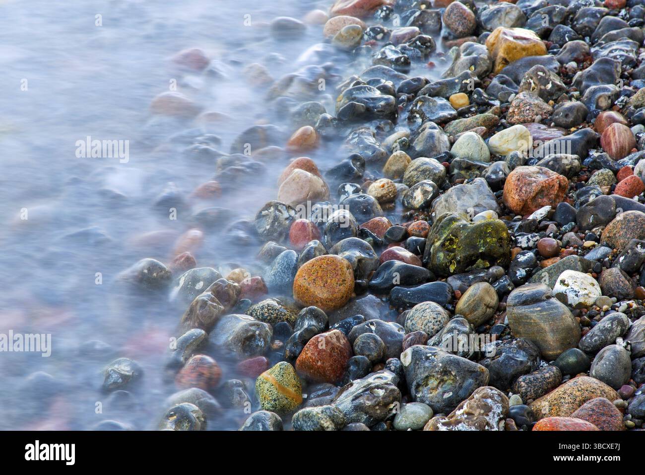 Blurred sea water of wave rolling over wet colourful pebbles on shingle ...