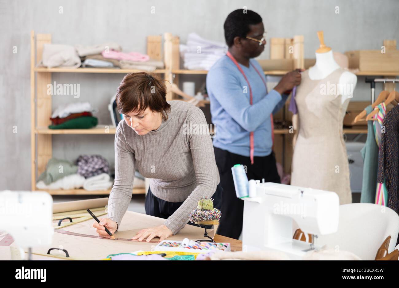 Female dressmaker sketching sewing pattern while colleague adjusting ...