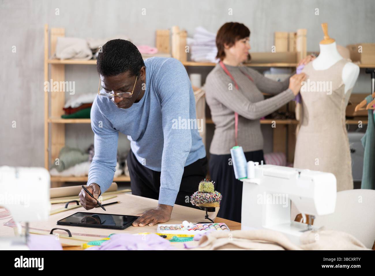 Fashion designer sketching garment on tablet while colleague working ...