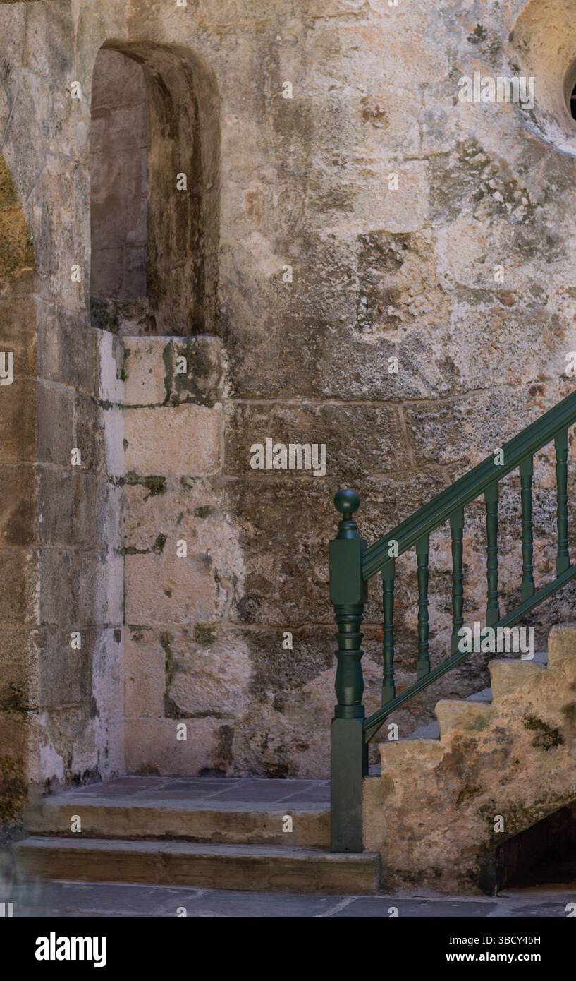 Rustic stone staircase with a dark green wooden railing leading to an ...
