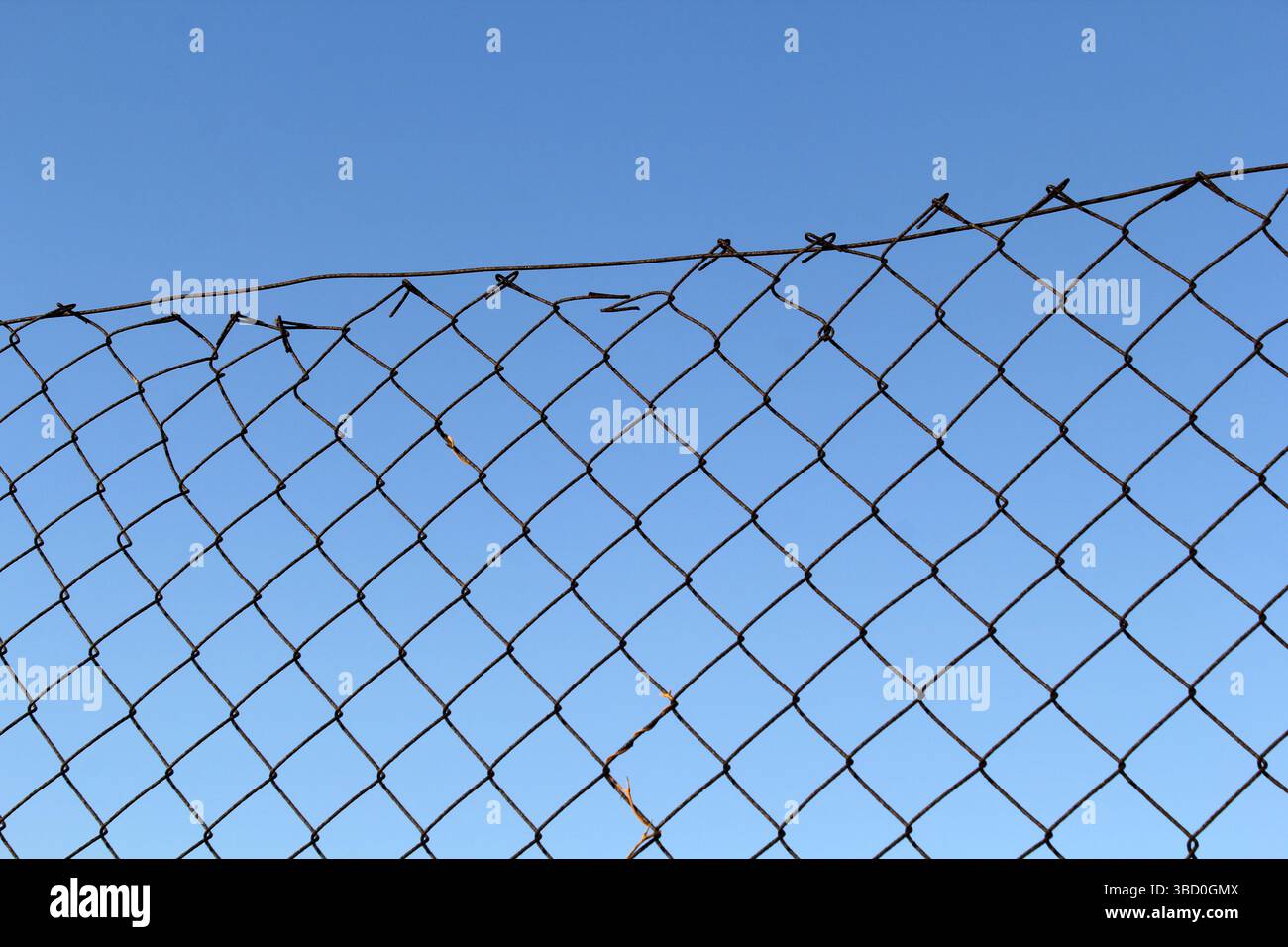 Damaged chain-link fence against a clear blue sky background Stock ...