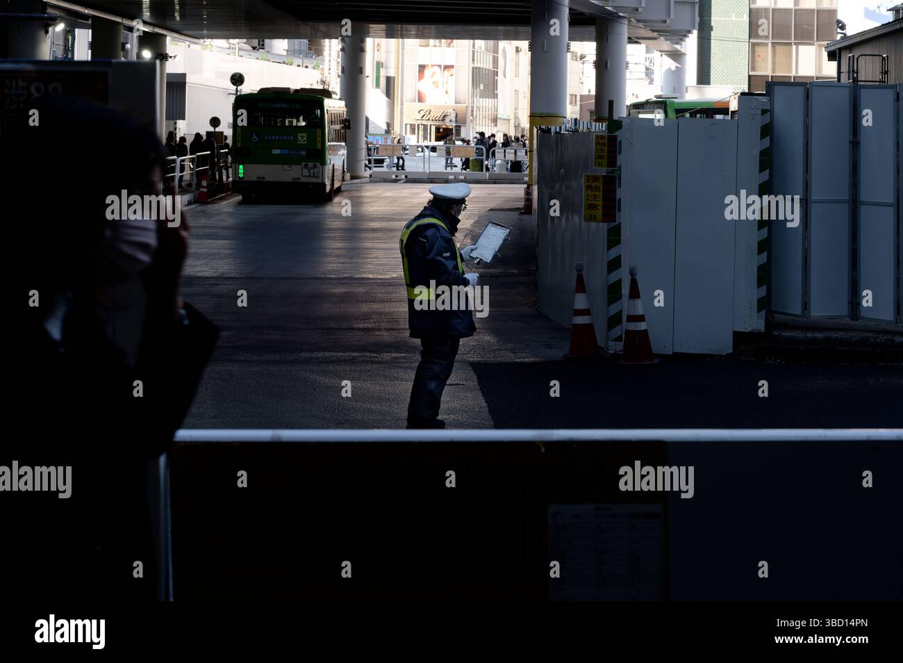 Lone traffic guard studies his clipboard at Shibuya’s bus terminal ...