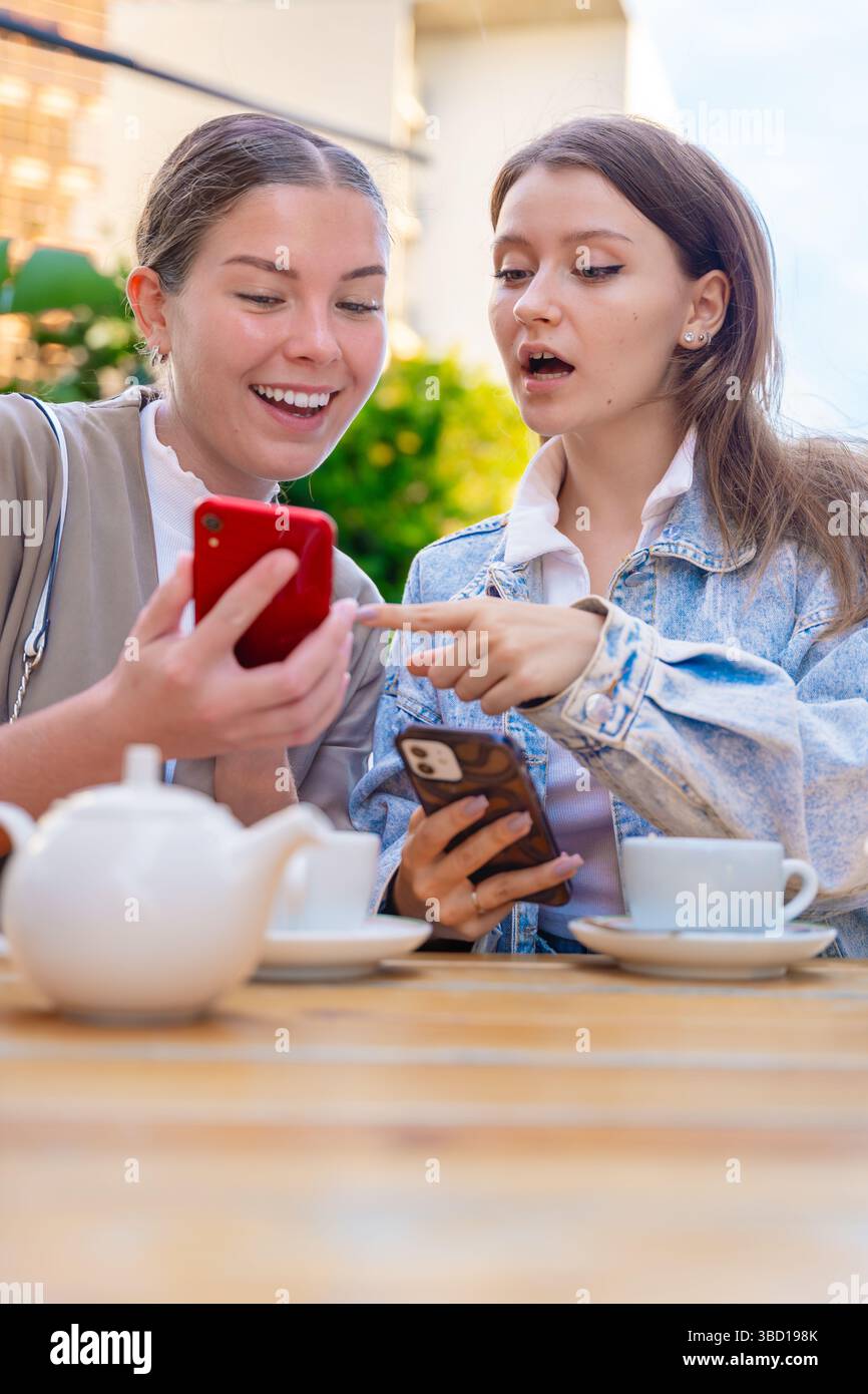 Teen girls laughing at cafe table while using smartphones during sunny day out Stock Photo - Alamy