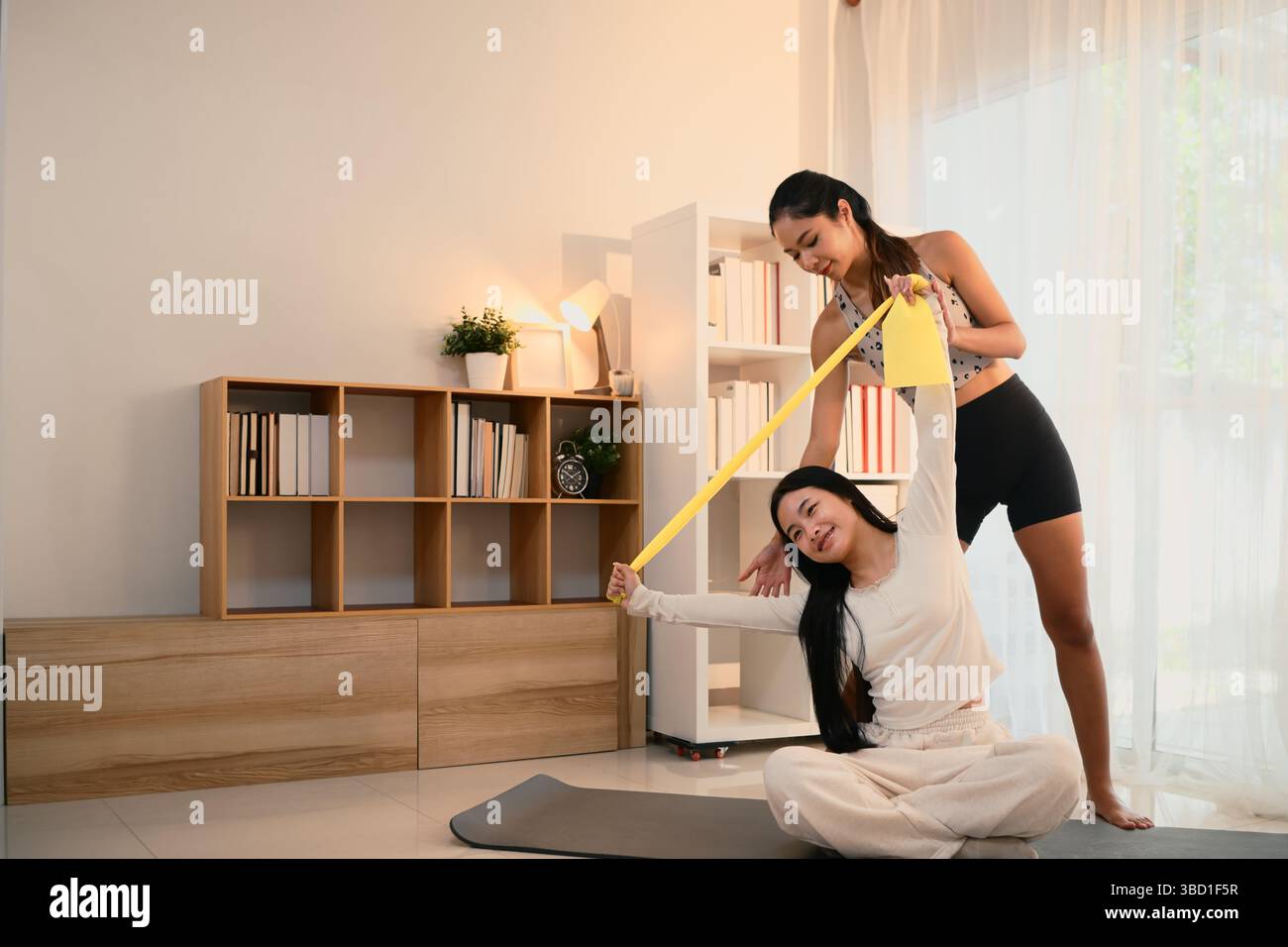 Active mother helping her daughter stretch with a resistance band in a ...