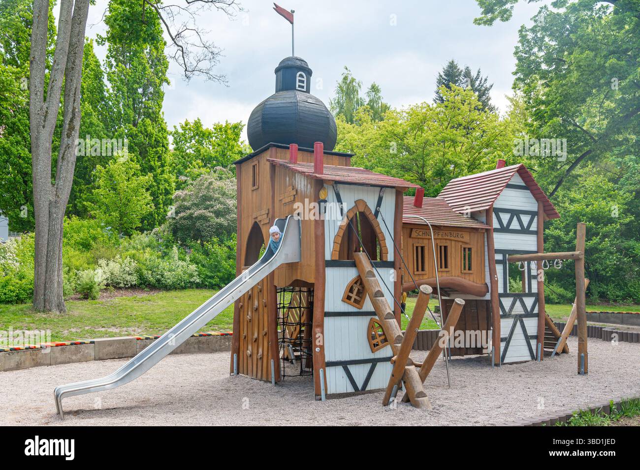 A child joyfully sliding down a playground slide within a themed wooden ...