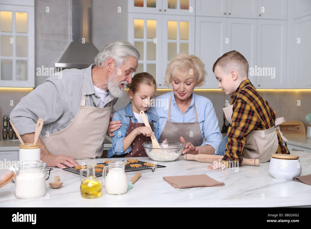 Grandparents and their grandkids cooking together at white marble table ...