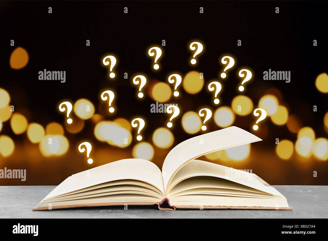 Question marks above open book on table against black background with ...