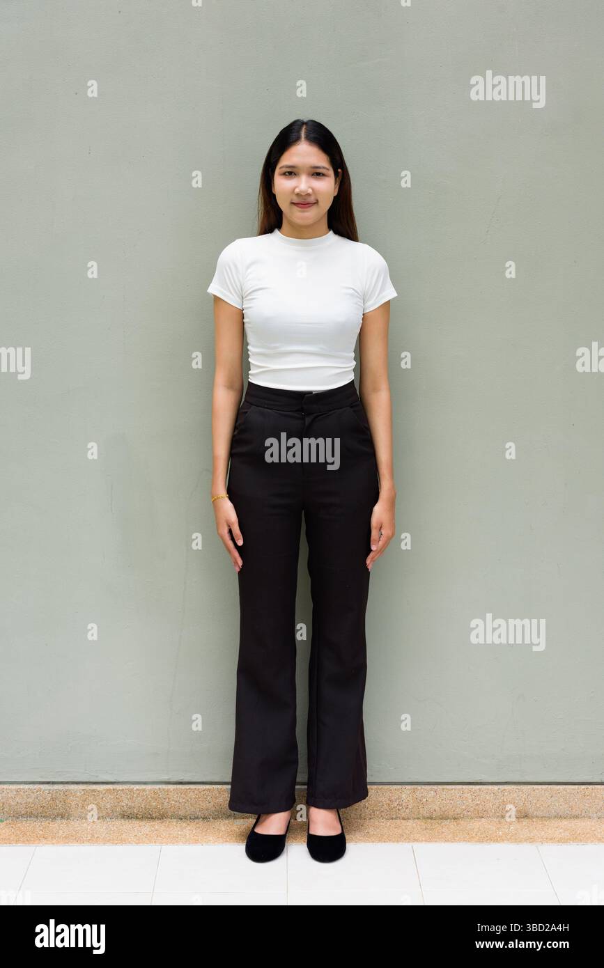 Portrait of young Asian woman standing wearing business clothes against ...