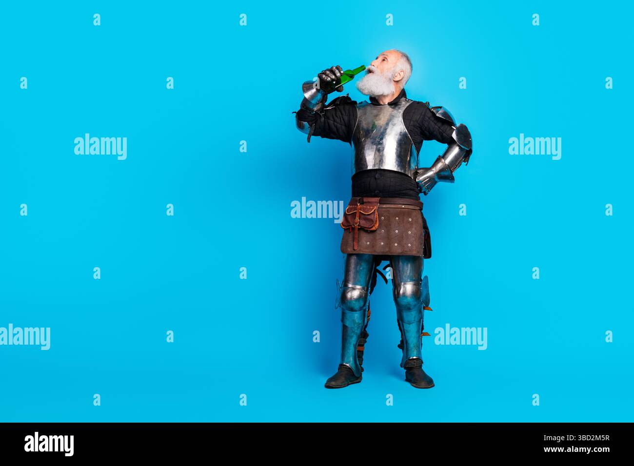Mature man in medieval knight armor drinking beverage against a blue ...