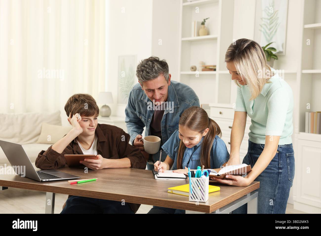 Happy parents and their children doing homework with laptop at table indoors Stock Photo - Alamy