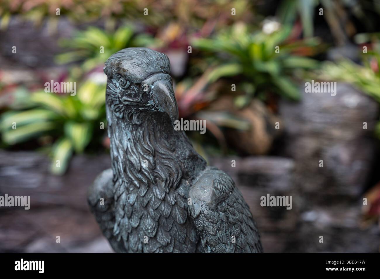 A bronze eagle statue in a Thai garden, surrounded by tropical plants ...