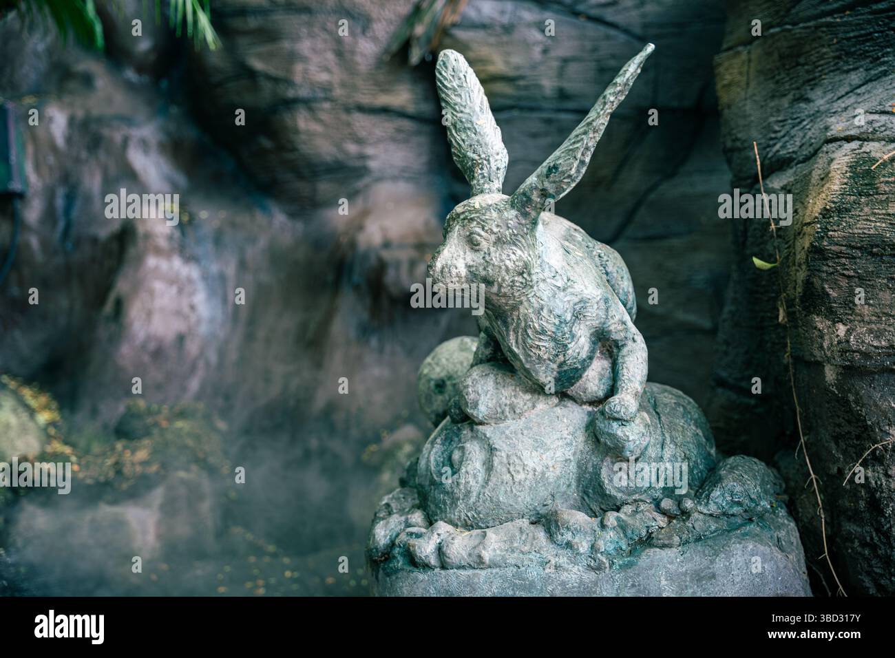 A bronze rabbit sculpture with long ears sits among mist and rocks in a ...