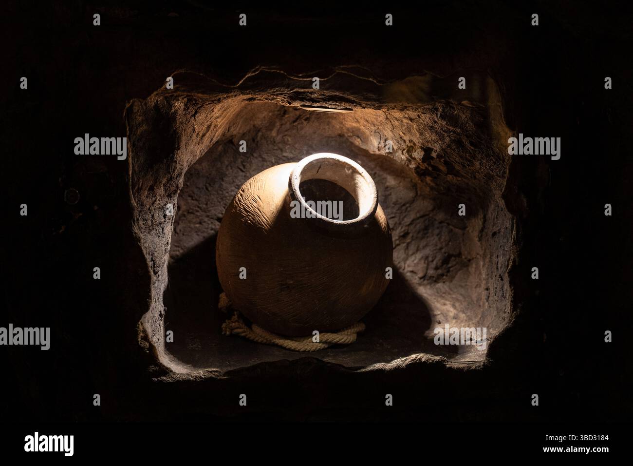 An old clay water pot displayed inside a temple cave niche, illuminated ...