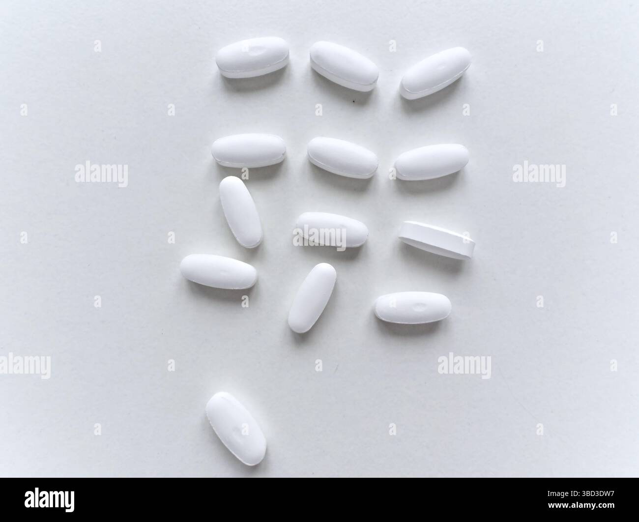 A row of white pills are scattered on a white surface. The pills are ...