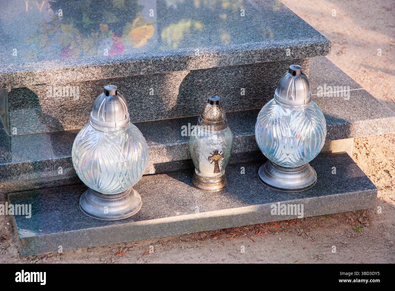 Three decorative glass lanterns on stone memorial in sunlit cemetery reflecting peaceful ...