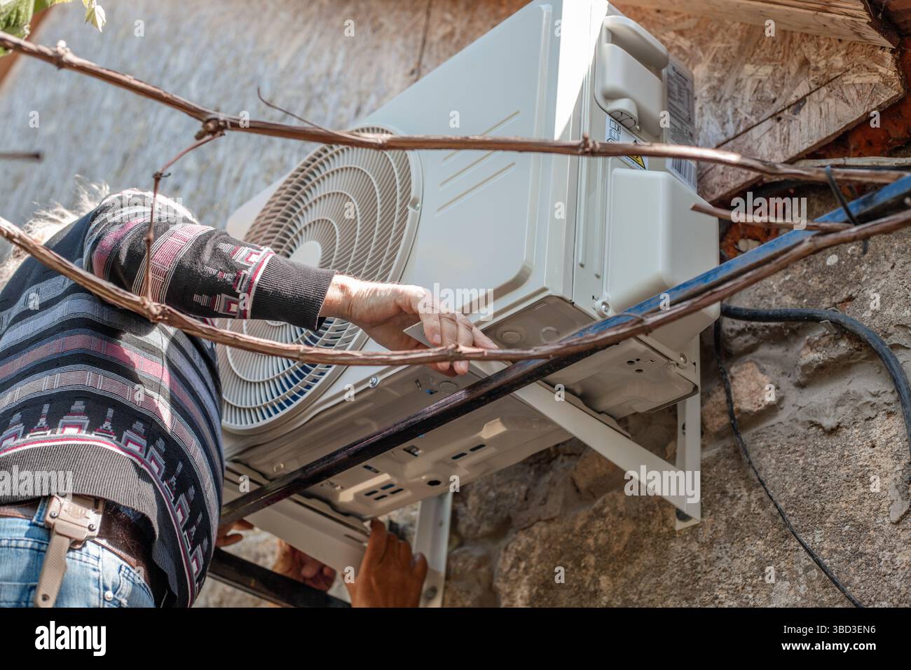 A man installs an outdoor air conditioner unit on iron mounting ...