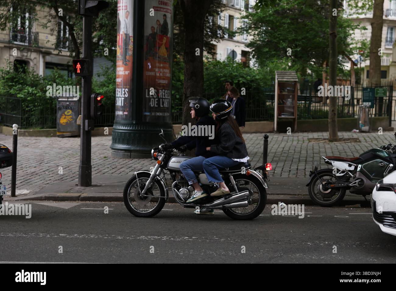Two riders on a motorcycle navigate through a busy urban street, both ...