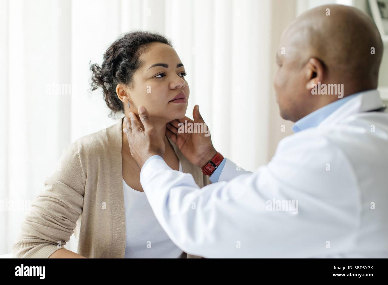 Black male doctor checking lymph nodes of female patient at hospital ...